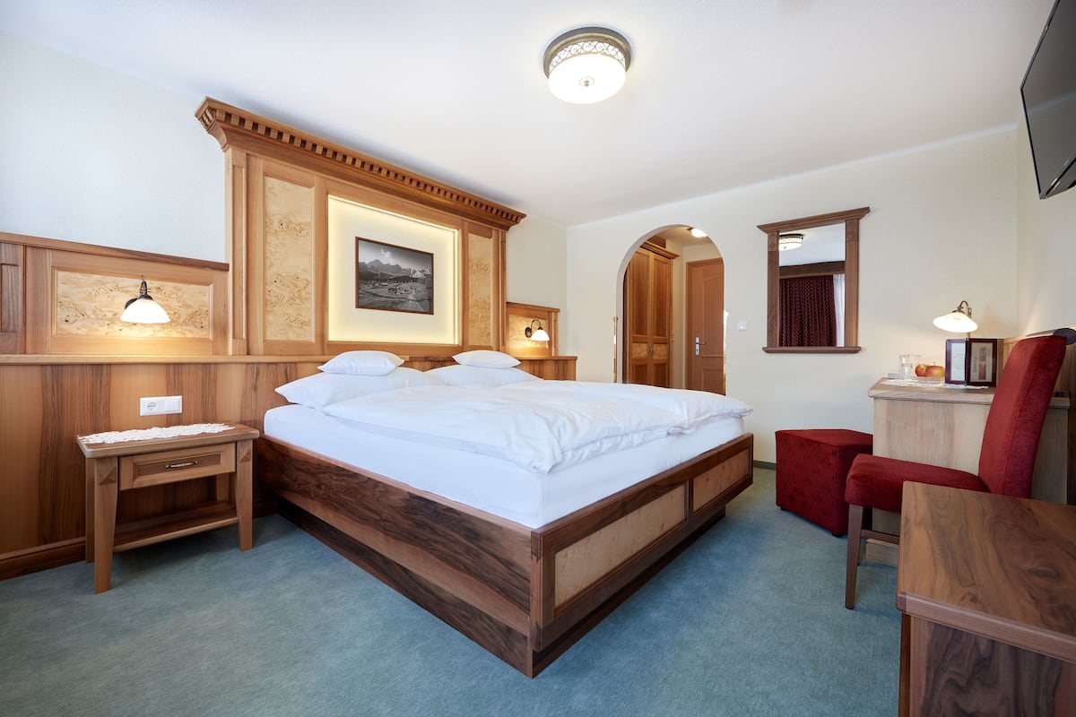 Quarto com cama grande, cabeceira de madeira, mesas de cabeceira, escrivaninha e uma cadeira.