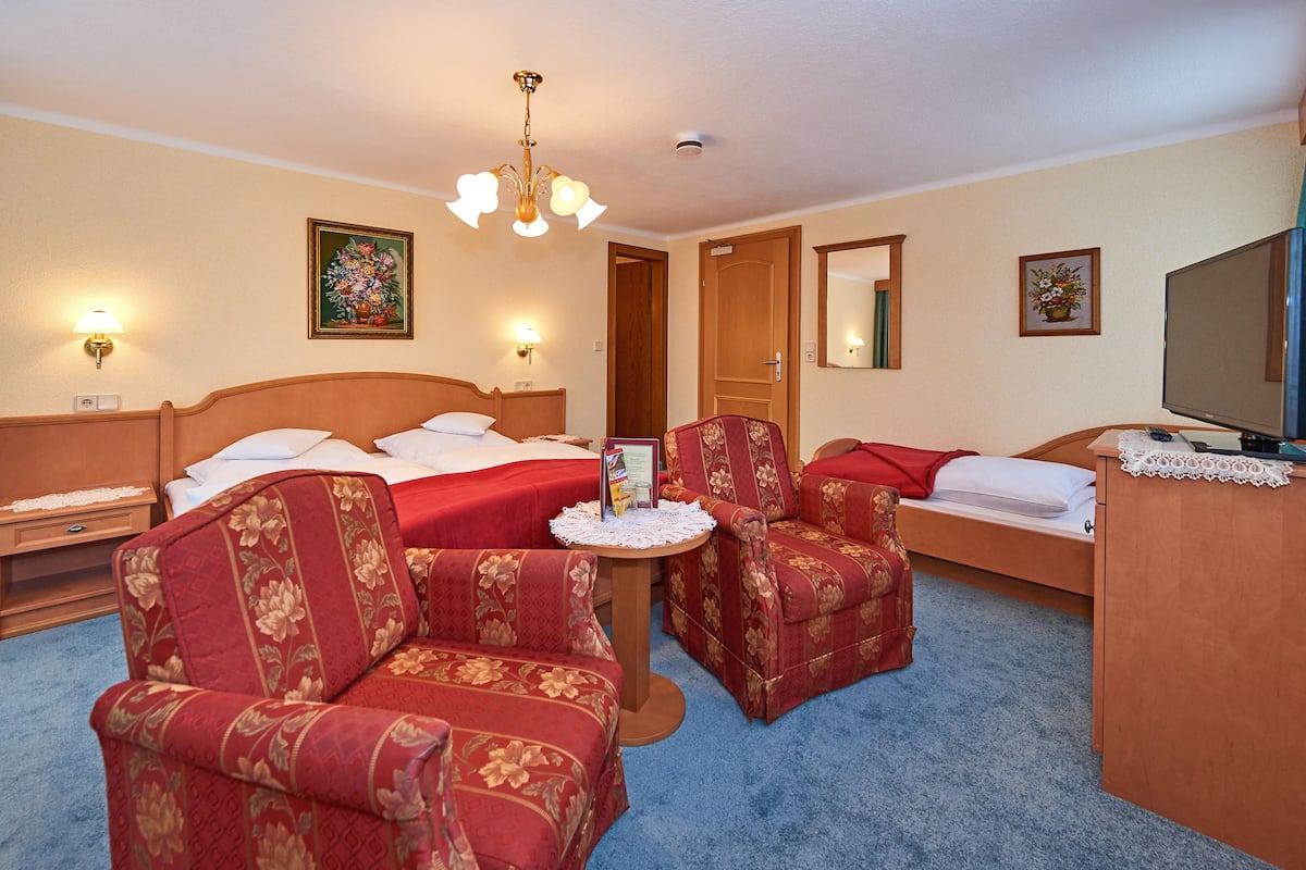 Quarto de hotel com cama, duas poltronas, uma mesinha, televisão e espelho.