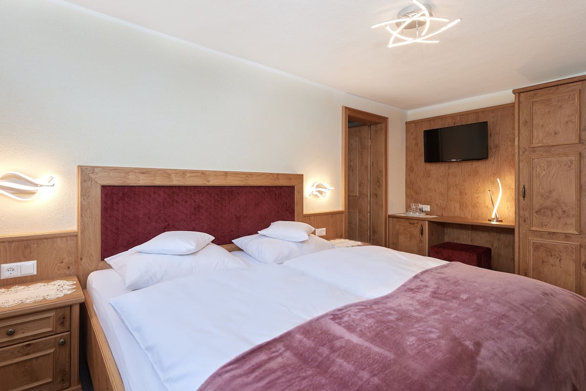 Quarto de hotel com uma cama grande, cabeceira de madeira, mesas de cabeceira, uma TV na parede e um guarda-roupa de madeira.