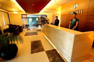 Uma área de recepção de hotel com um balcão de mármore, um vaso de planta e um espaço de estar com mesas e cadeiras.