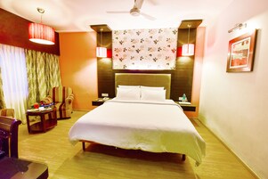 Quarto de hotel com uma cama grande, uma escrivaninha, uma cadeira, um criado-mudo e um ventilador de teto.
