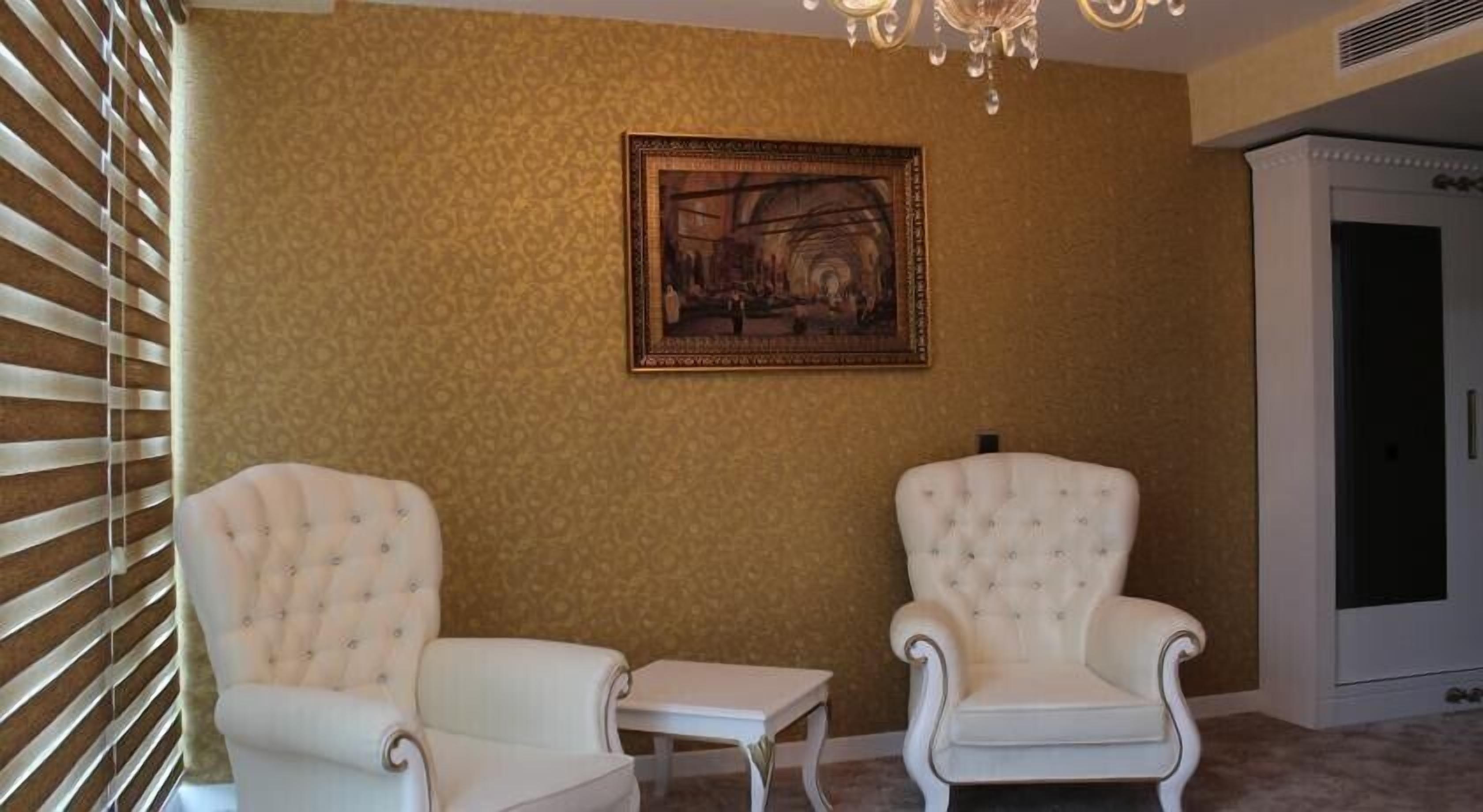 Quarto com duas poltronas brancas, uma pequena mesa branca e um quadro emoldurado na parede.