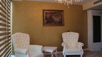 Quarto com duas poltronas brancas, uma pequena mesa branca e um quadro emoldurado na parede.
