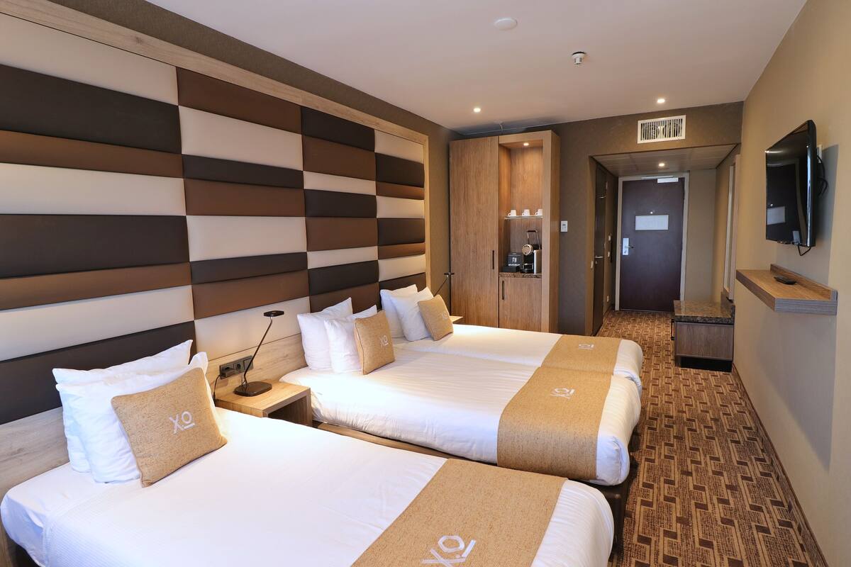 Quarto de hotel com duas camas, televisão, minibar e banheiro visível por uma porta aberta.