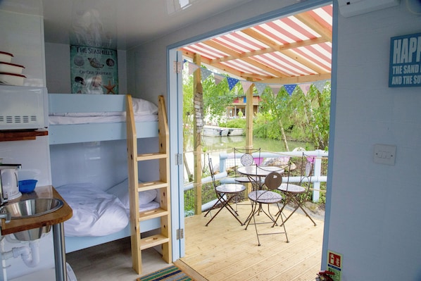Quarto compacto com beliches, uma kitchenette pequena e vista para um jardim com área de estar ao ar livre.