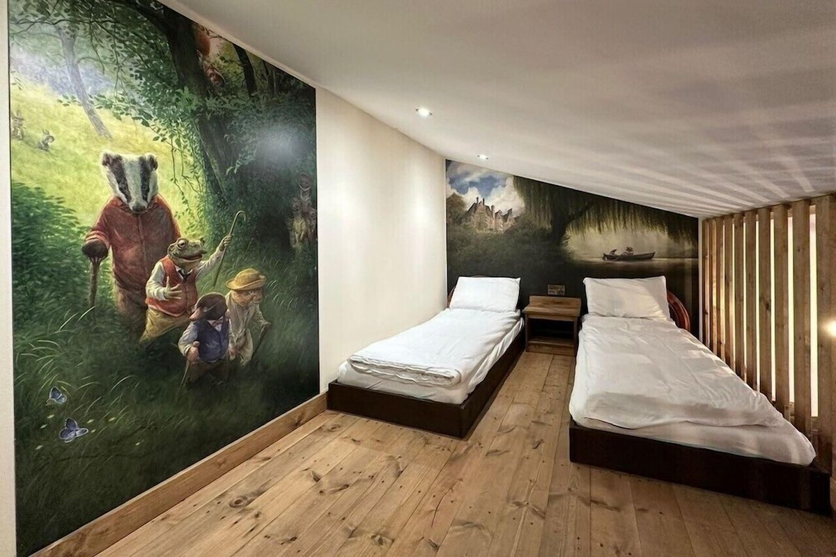 Quarto com duas camas, um mural de animais da floresta, piso de madeira e parede de ripas de madeira.
