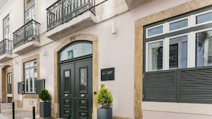 Fachada de edifício com uma porta dupla preta, varanda com grades de ferro forjado e uma placa na parede.