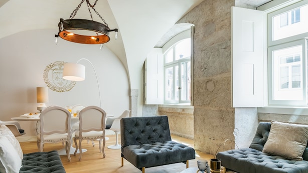 Uma sala de estar moderna com um sofá estofado, uma mesa de centro redonda e uma área de jantar com cadeiras brancas e uma mesa.