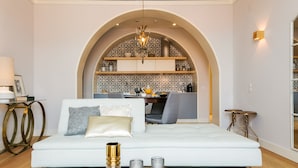 Uma sala de estar moderna com um sofá branco, uma mesa de centro e uma cozinha ao fundo.