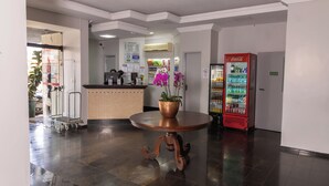 Um hall de entrada com uma mesa de recepção, uma geladeira vermelha Coca-Cola e um vaso de planta.