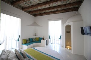 Quarto com cama curva, um espaço de estar pequeno com televisão e varanda com vista.