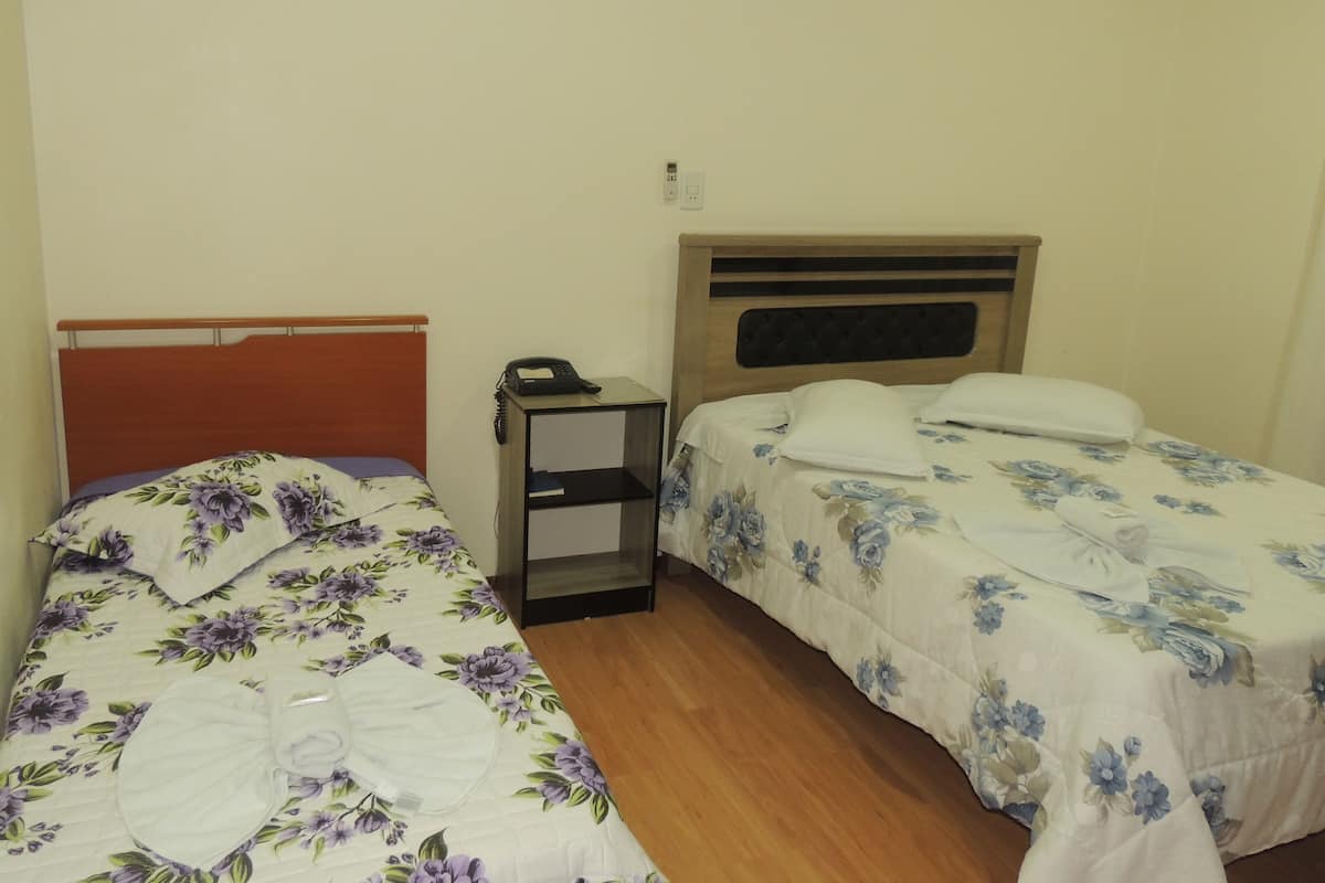 Quarto com duas camas, cada uma com roupa de cama floral, uma mesinha de cabeceira com telefone e uma estante.