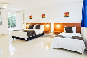 Quarto de hotel com duas camas, cada uma com cabeceira de madeira e luminárias laterais. Há três quadros pendurados na parede acima das camas.