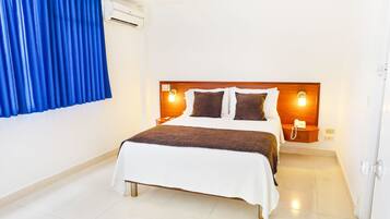 Quarto de hotel com cama, mesa de cabeceira, abajur, telefone e janela com cortinas azuis.