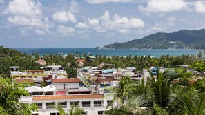Uma cidade costeira com edifícios, palmeiras e vista para o mar e colinas.