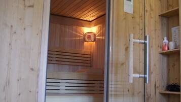 Uma sala de sauna com paredes de madeira e porta de vidro, um banco e uma prateleira com garrafas.