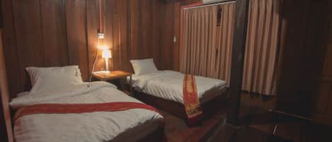 Quarto com duas camas, uma mesa de cabeceira com abajur, paredes de madeira e cortina.
