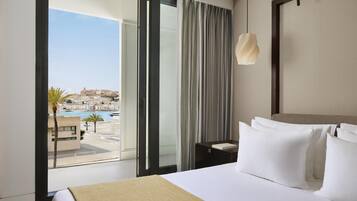 Quarto de hotel com cama, mesa de cabeceira, luminária e vista para o horizonte costeiro.