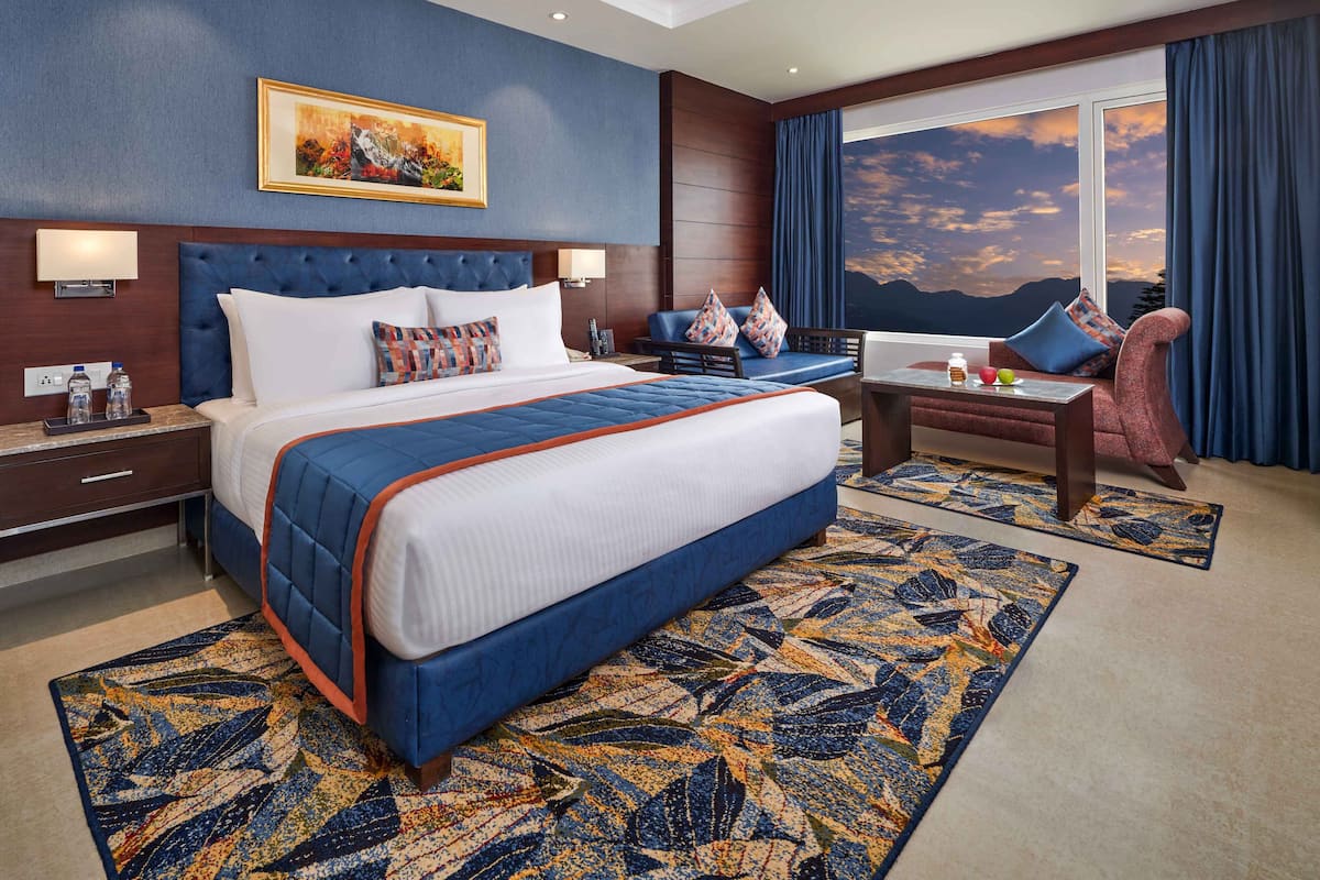 Quarto de hotel com uma cama grande, um sofá, uma mesa de trabalho e vista para as montanhas.