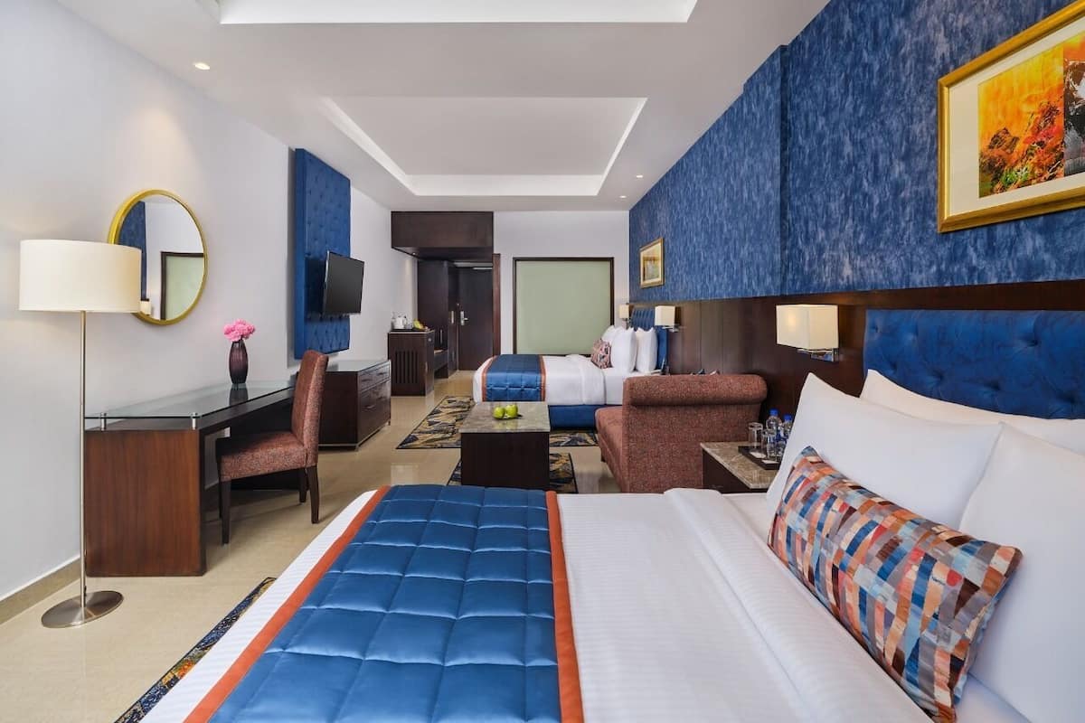 Quarto de hotel com uma cama grande, uma escrivaninha, uma cadeira, um sofá e uma televisão.