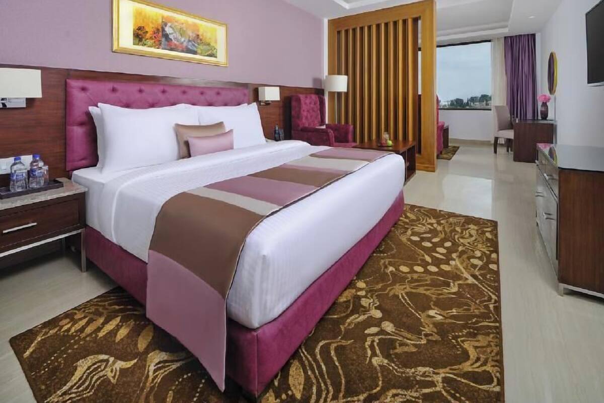 Quarto de hotel com uma cama grande, mesa de cabeceira, escrivaninha, cadeira, televisão e janela com cortinas.