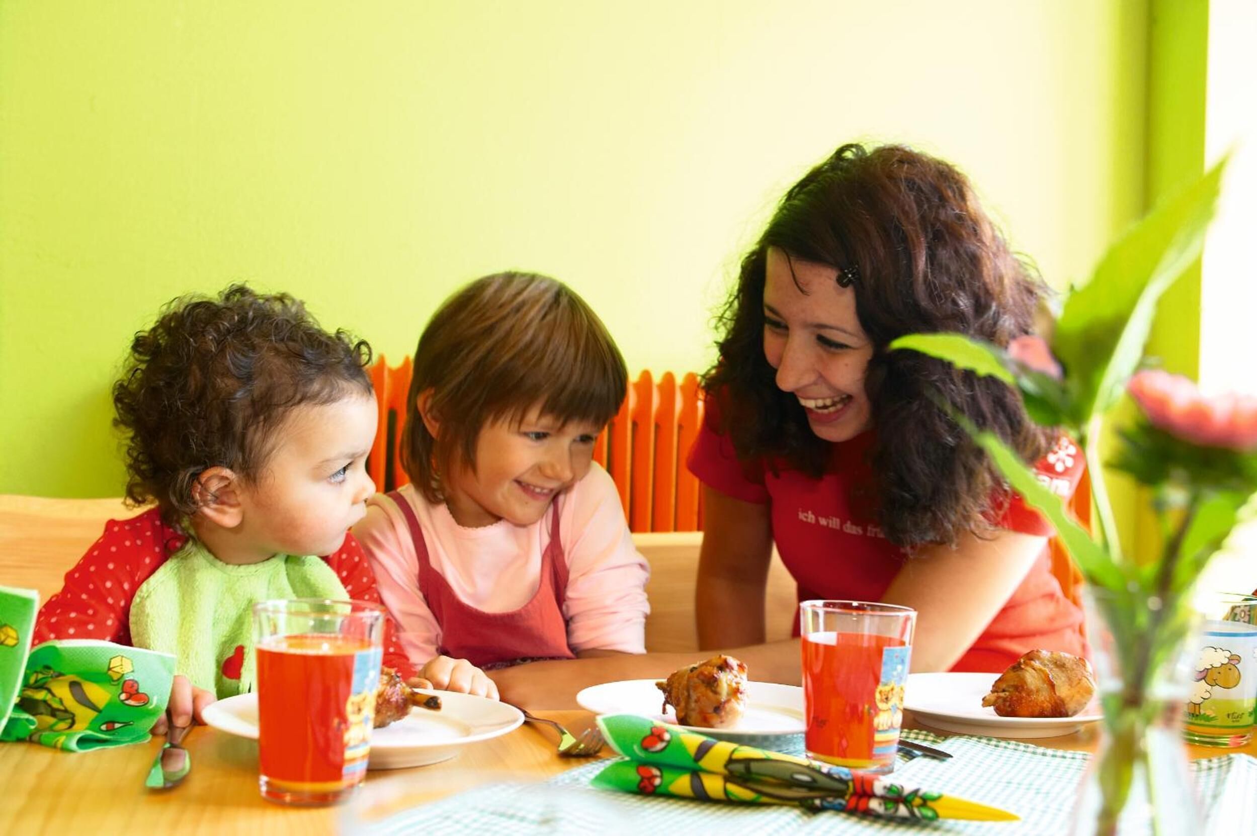 Três pessoas sentadas à mesa, com comida e bebidas.