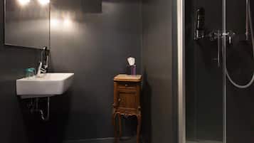 Um banheiro moderno com pia branca, toucador de madeira e box de vidro.