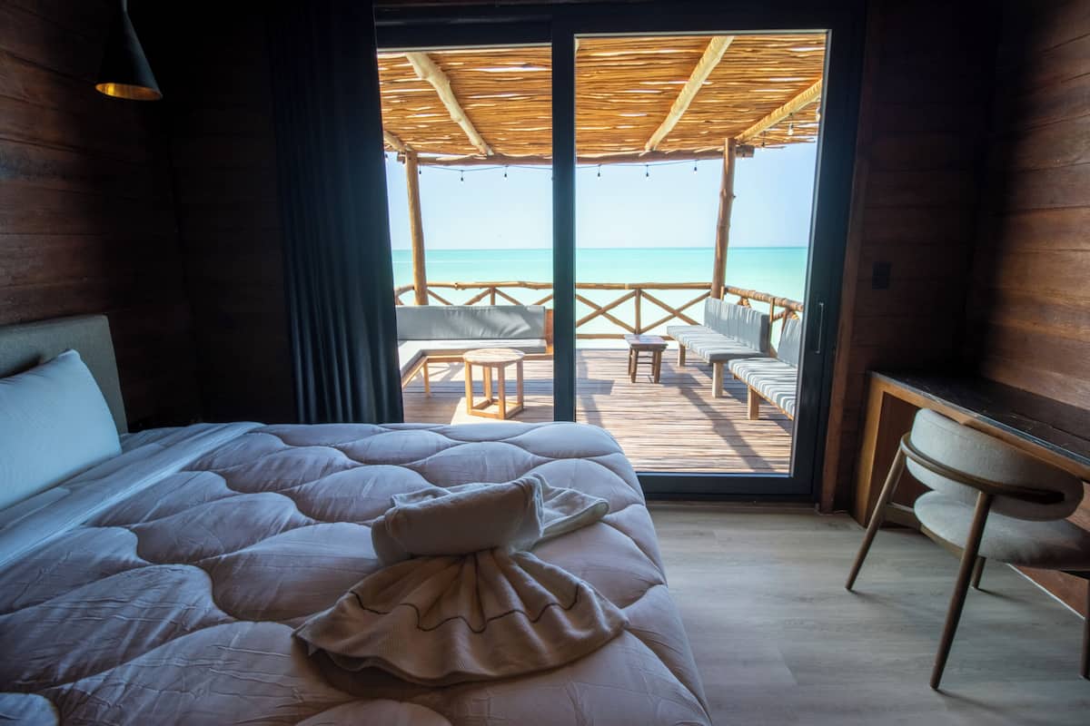 Quarto com uma cama grande, uma escrivaninha de madeira e vista para o oceano.