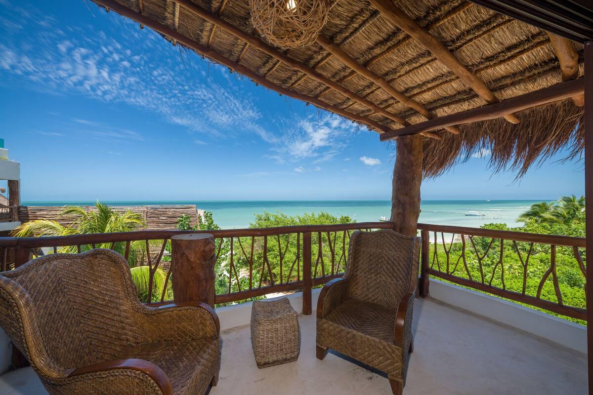 Uma área de estar coberta ao ar livre, com móveis de vime e vista para o oceano.
