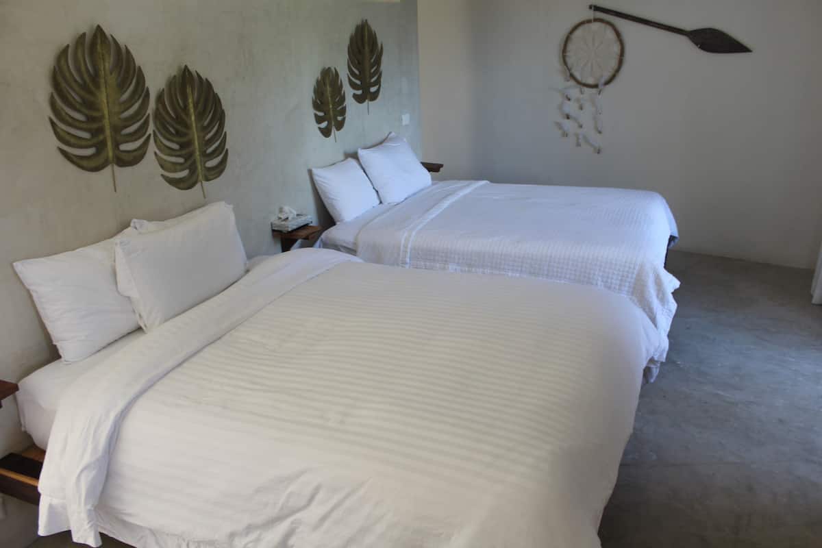 Quarto com duas camas, roupa de cama branca e decoração de parede incluindo folhas e um sonho capturado.