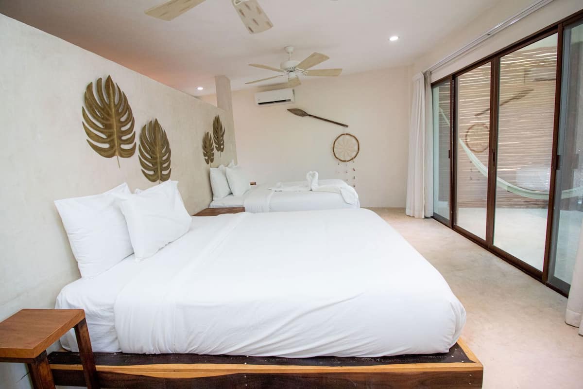 Quarto moderno com cama grande, ventilador de teto e vista através de uma porta de vidro.