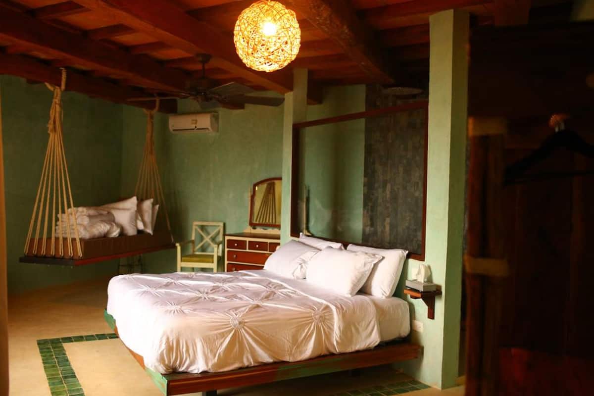 Quarto com cama, cadeira suspensa, espelho e luminária pendente.