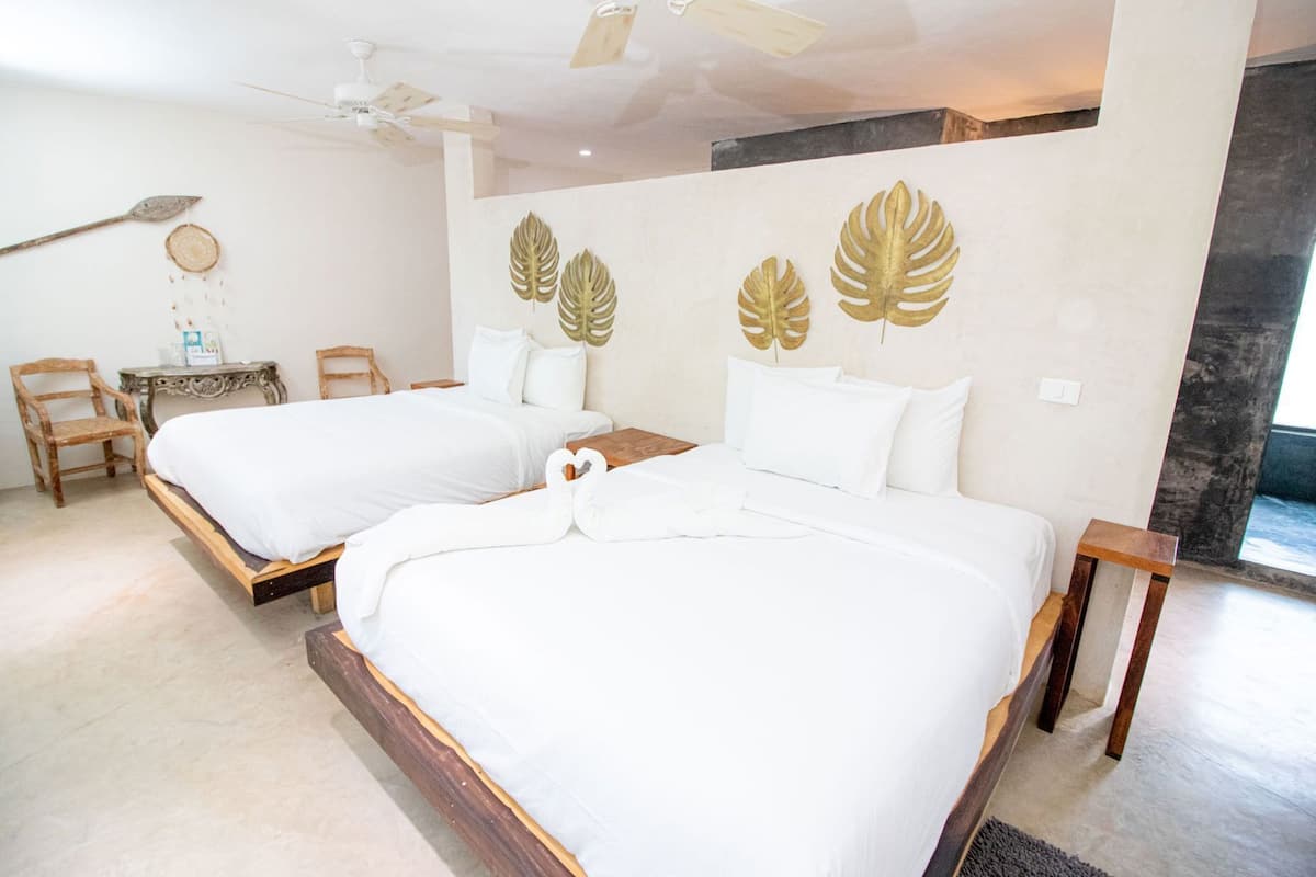 Quarto de hotel com duas camas, móveis de madeira, ventoinha no teto e detalhes decorativos nas paredes.