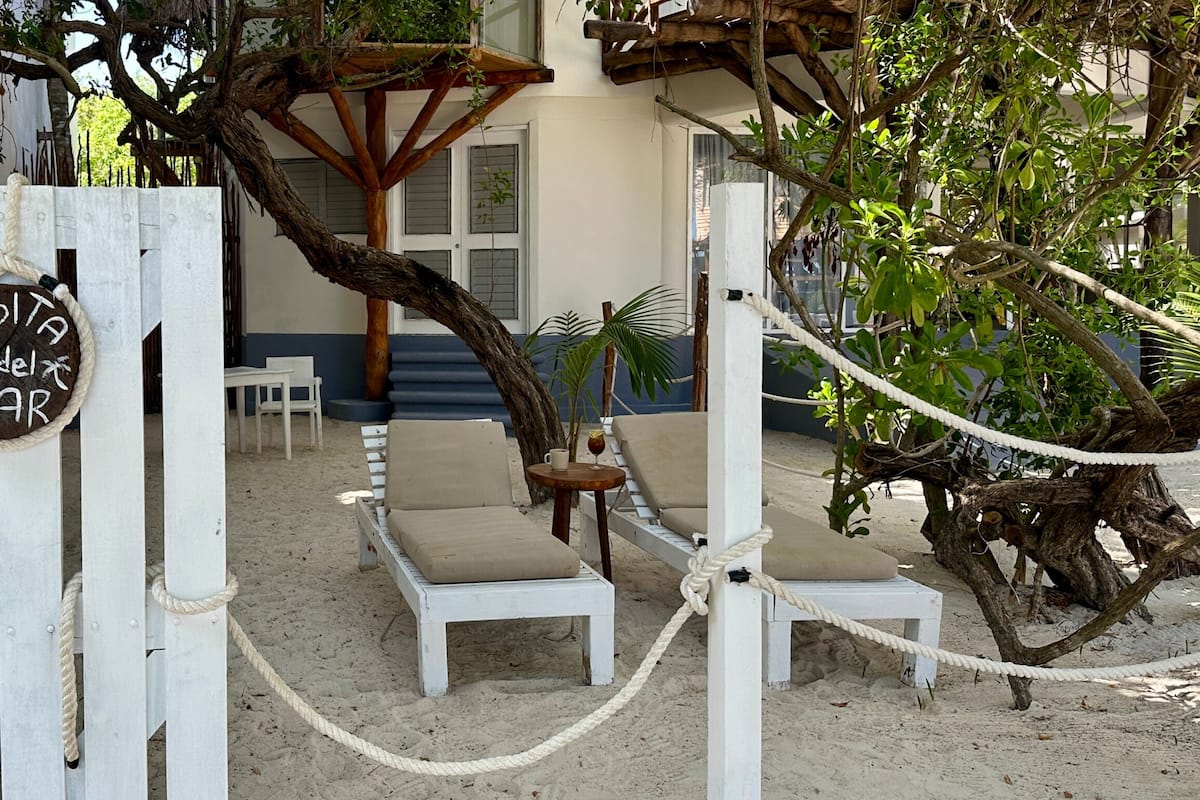 Uma área de estar à beira-mar, com cadeiras de lounge brancas e uma placa de madeira com a inscrição "CASITA del mar".