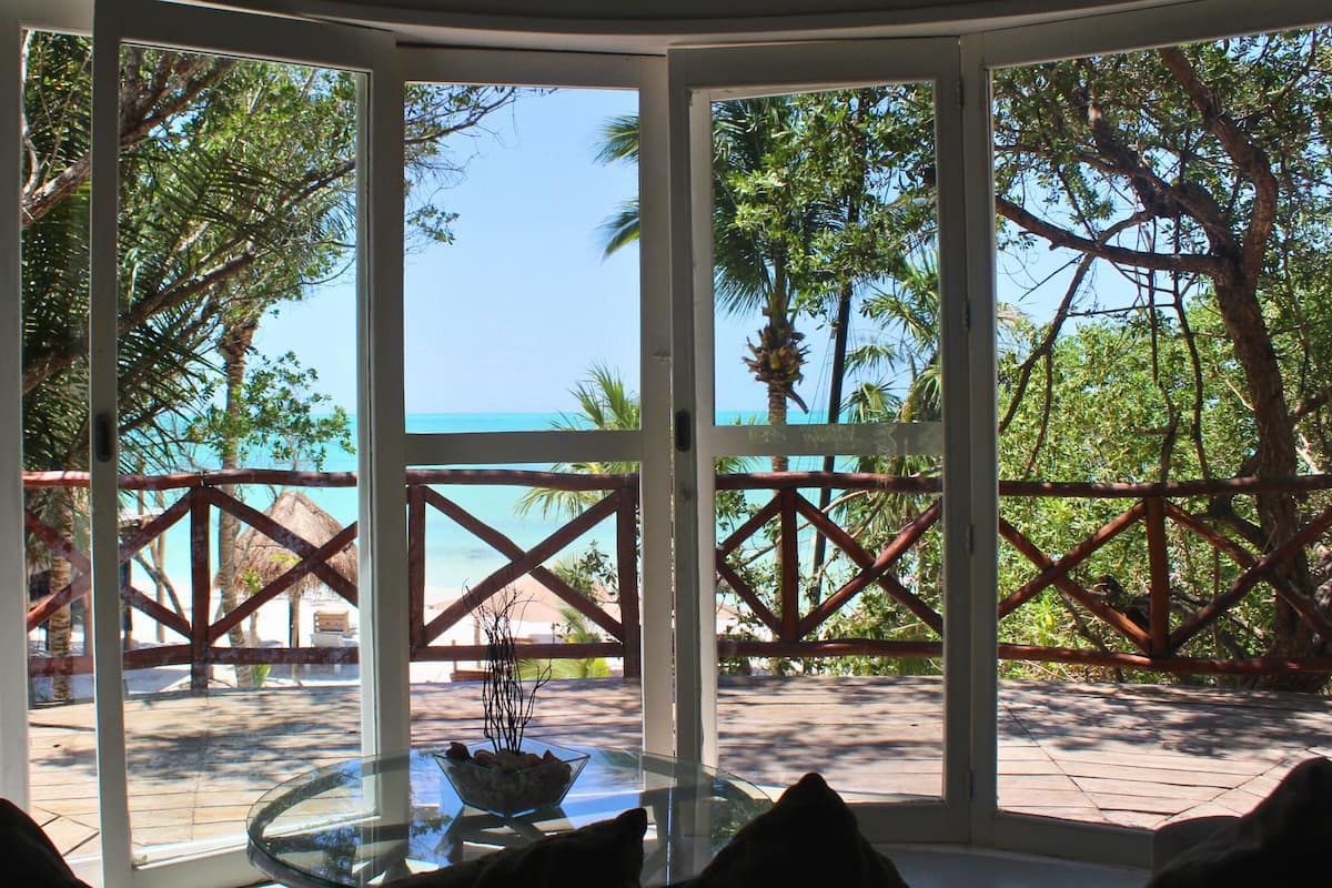Um espaço envidraçado com vista para o oceano e palmeiras.