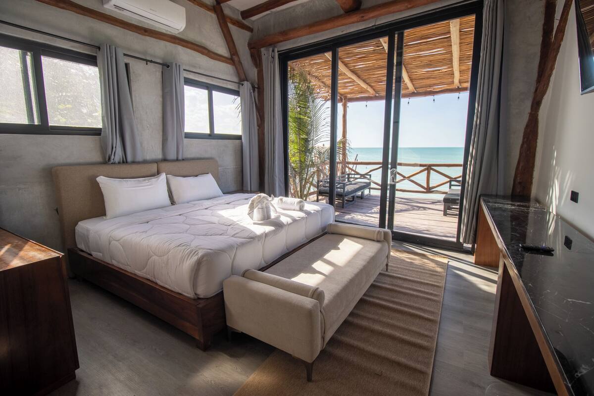 Quarto com cama, banco e vista para o oceano.