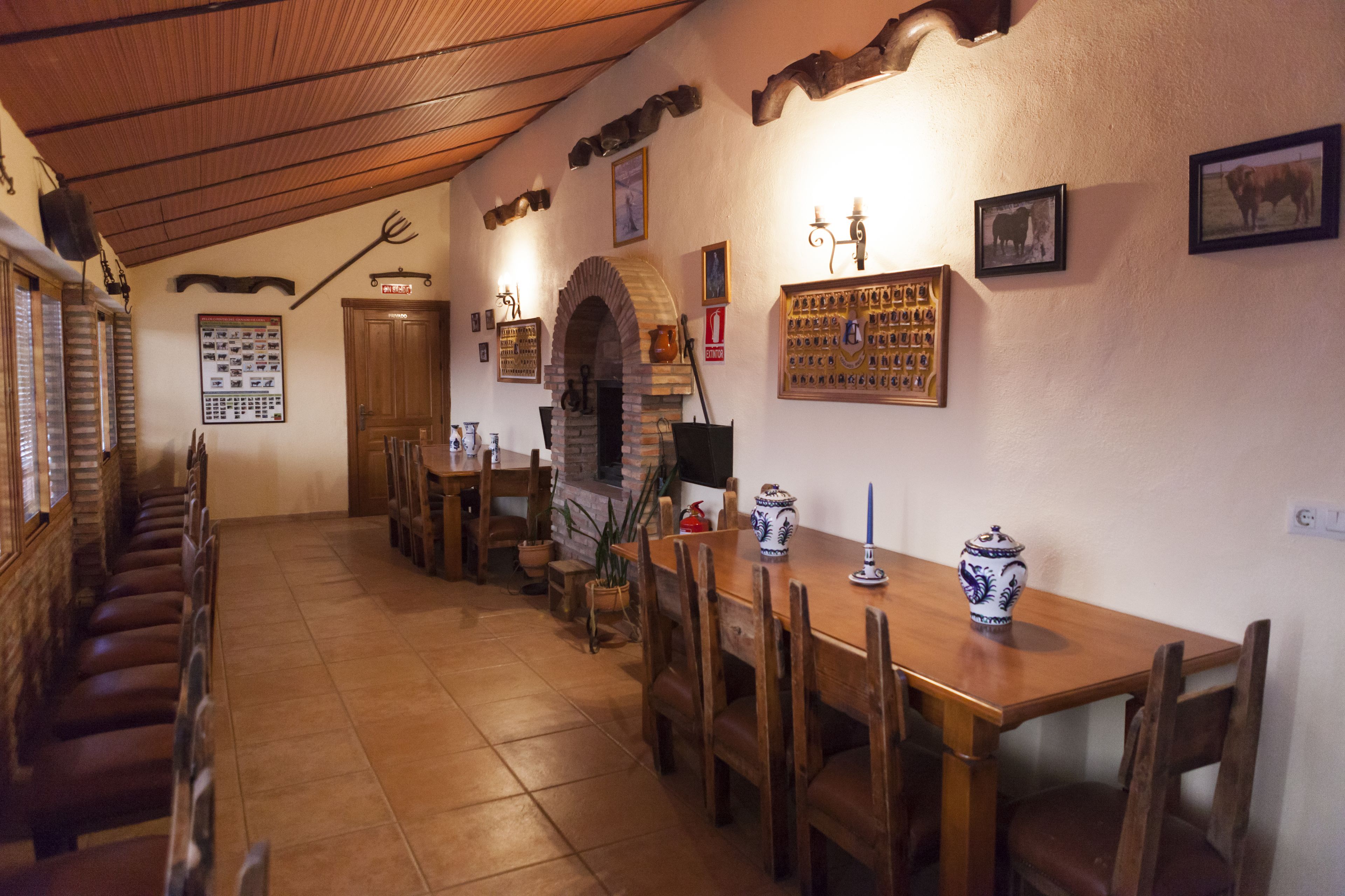Uma sala de jantar com uma longa mesa de madeira, cadeiras, uma lareira de pedra e várias decorações nas paredes, incluindo quadros e um quadro de menu.
