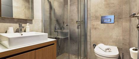 Um banheiro moderno com box de vidro, pia branca com armário de madeira e vaso sanitário com suporte para toalhas de papel.