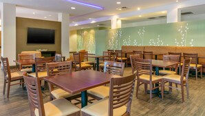 Um restaurante com mesas e cadeiras de madeira, uma TV de tela plana e painéis decorativos na parede.