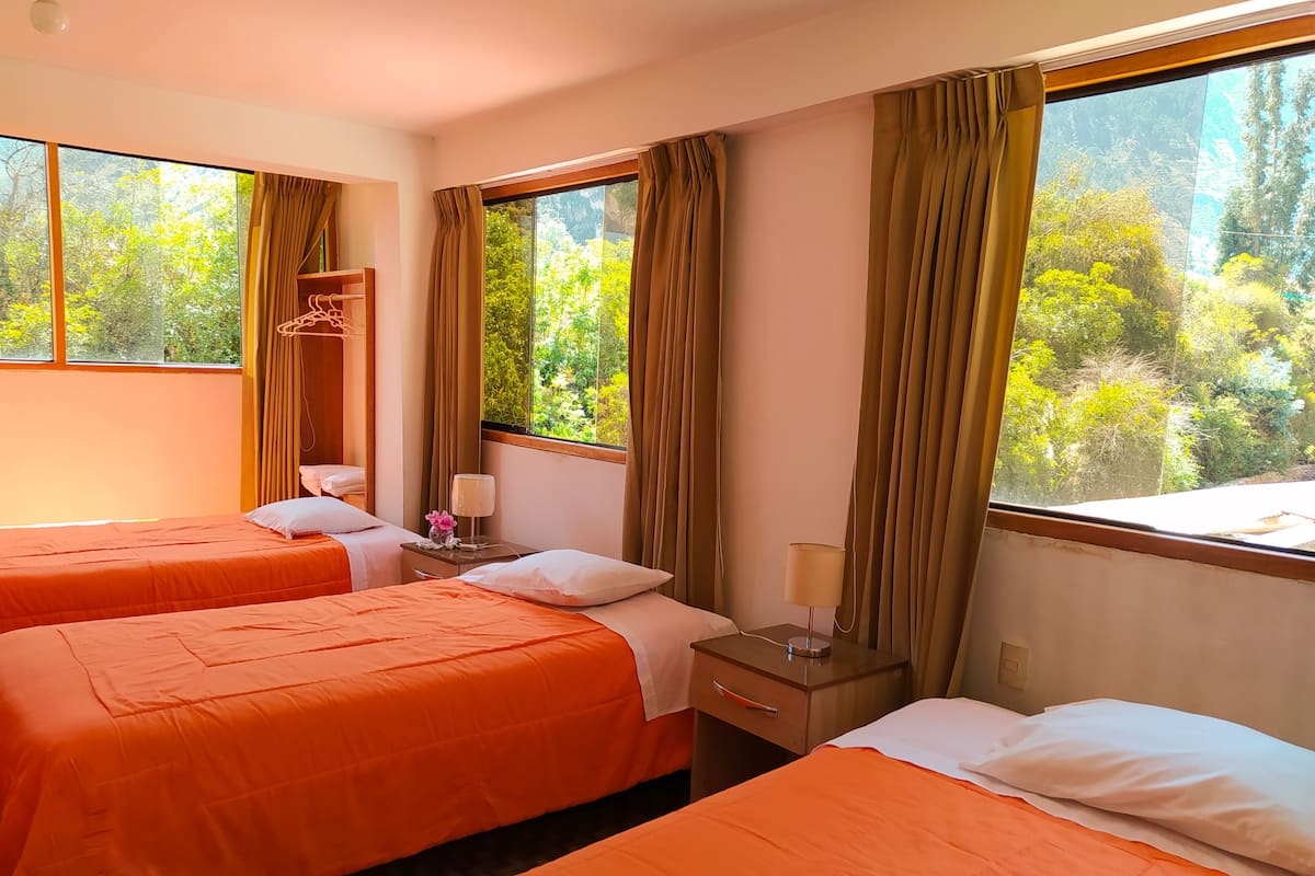 Quarto de hotel com duas camas, uma mesa de cabeceira, uma luminária e vista para o verde lá fora.