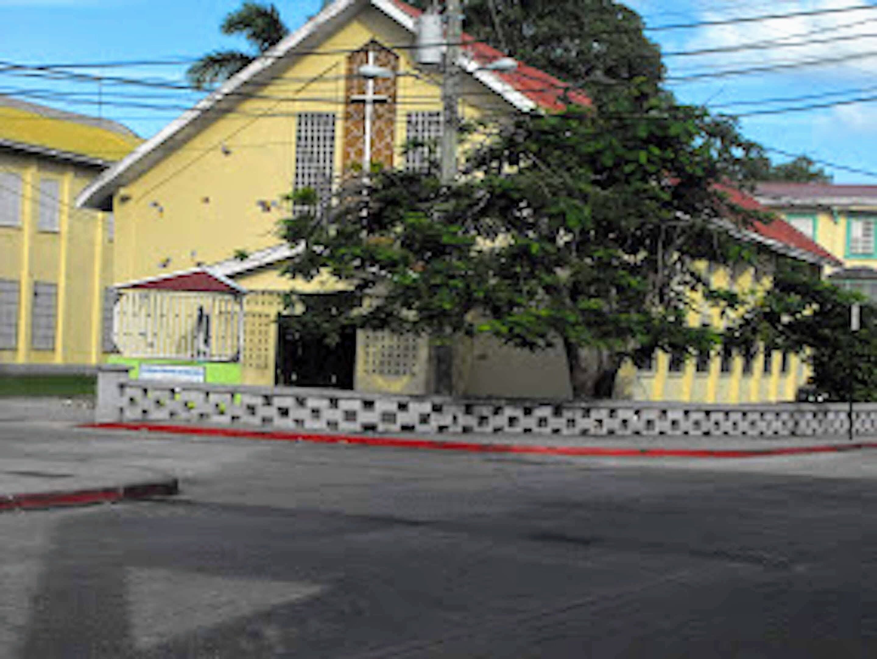 Um edifício amarelo com telhado vermelho, uma cruz e uma cerca.