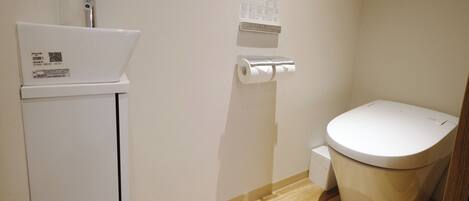 Uma casa de banho pequena e limpa, com sanita, lavatório e dispensador de papel.