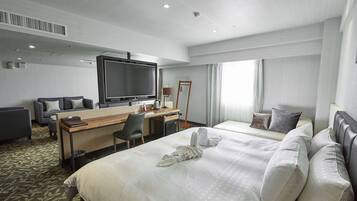 Quarto de hotel com cama, escrivaninha, televisão e uma janela grande.