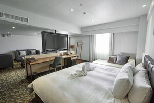 Quarto de hotel com cama, escrivaninha, televisão e uma janela grande.