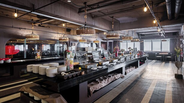 Um restaurante moderno com um balcão comprido, várias estações de atendimento e luminárias pendentes.