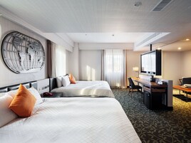 Quarto de hotel com duas camas, uma escrivaninha, uma televisão e um mapa-múndi grande na parede.