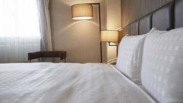 Quarto de hotel com cama arrumada, abajur e uma cadeira.