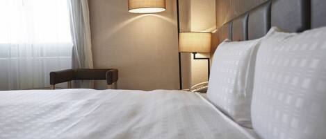 Quarto de hotel com cama arrumada, abajur e uma cadeira.