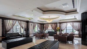 Um hall amplo com área de estar espaçosa, um candelabro e grandes janelas com cortinas.