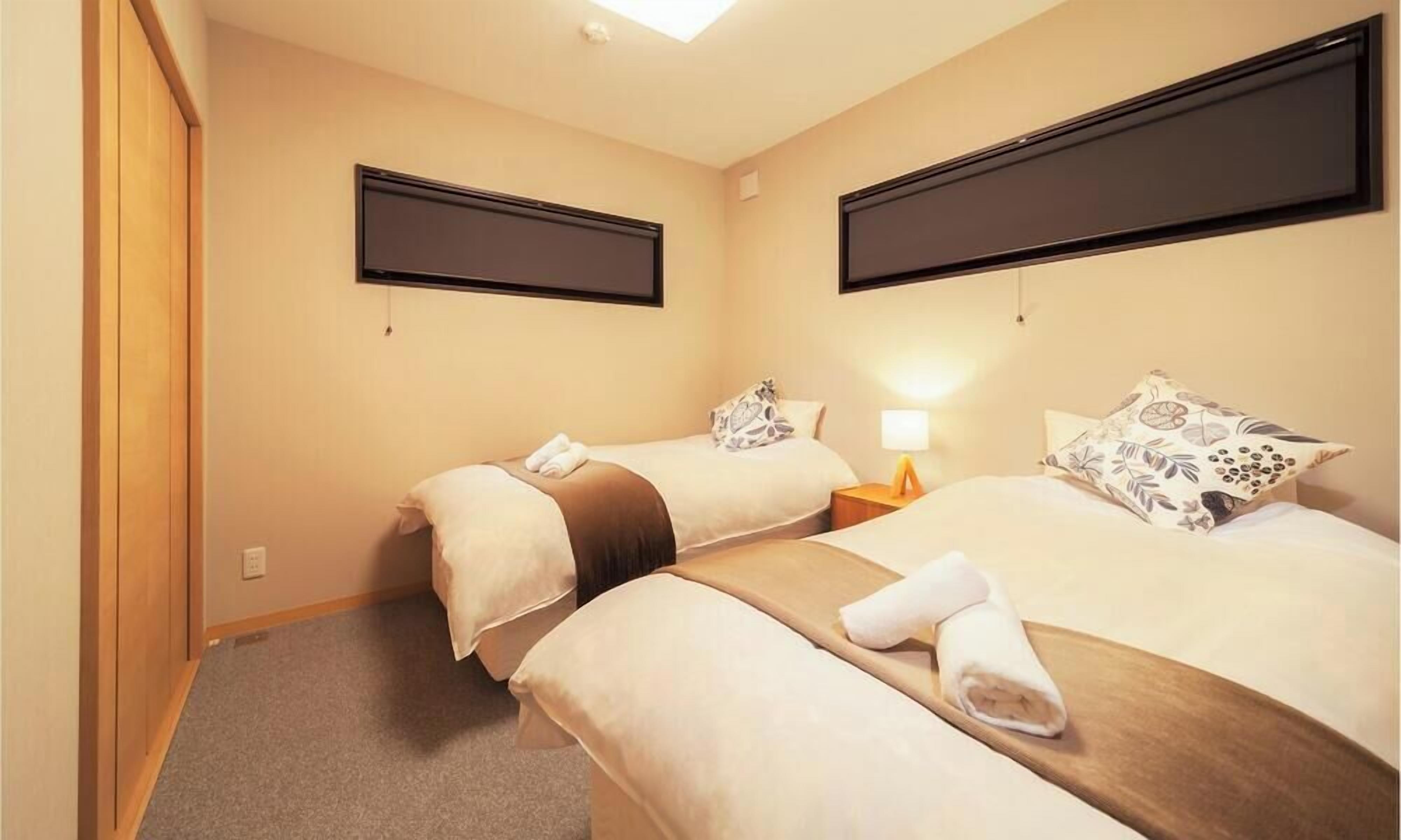 Quarto de hotel com duas camas, uma luminária no teto e uma janela.